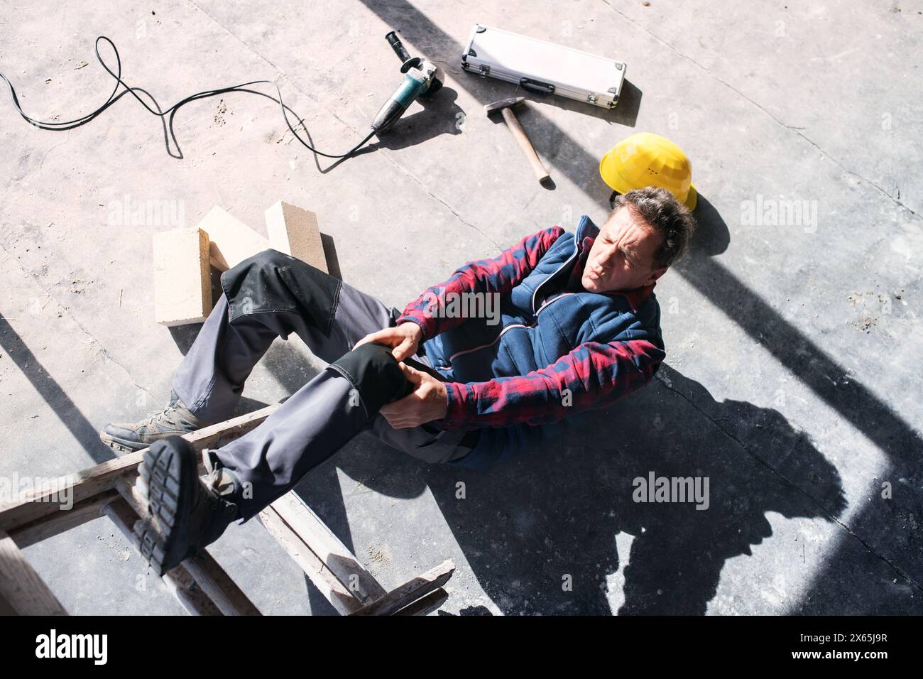 Male worker lying on the floor after fall from ladder, holding his knee ...