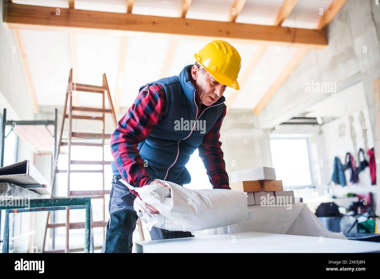 Older worker carrying heavy bag with building material. Work injury ...