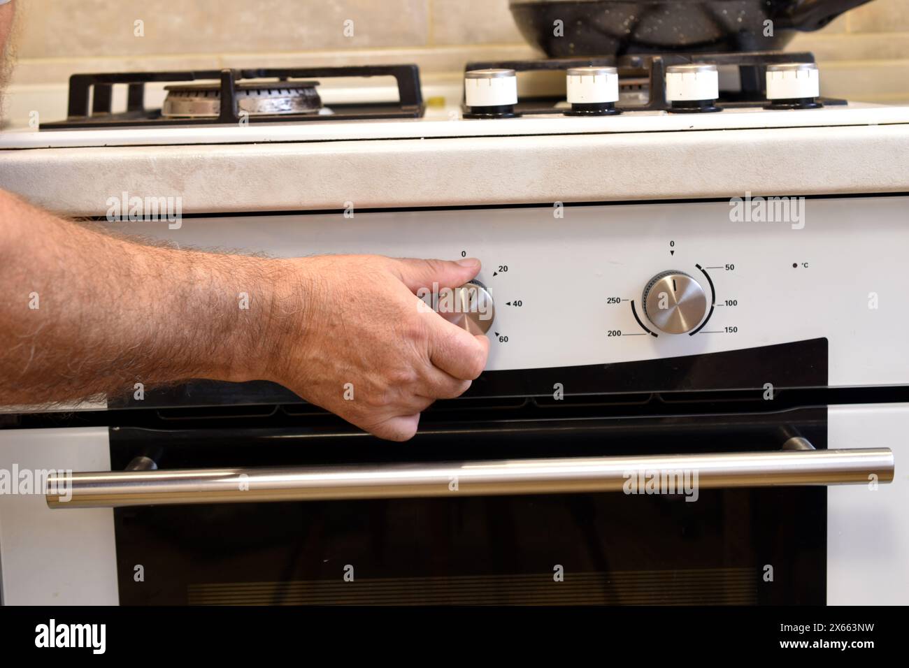 The picture shows a man's hand turning the oven timer knob to the ...