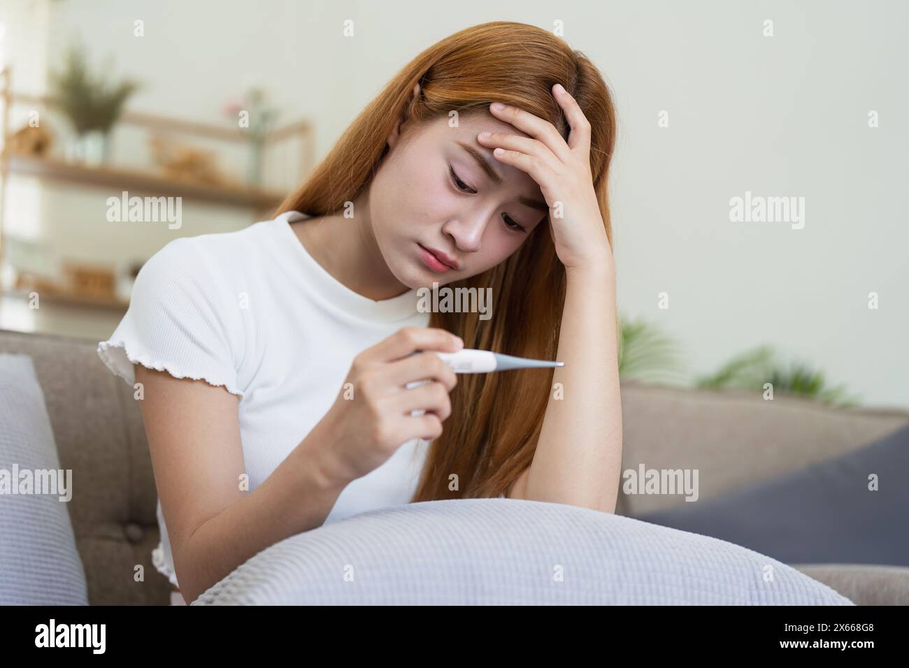 Sick young asian woman with thermometer suffering from cold on sofa ...