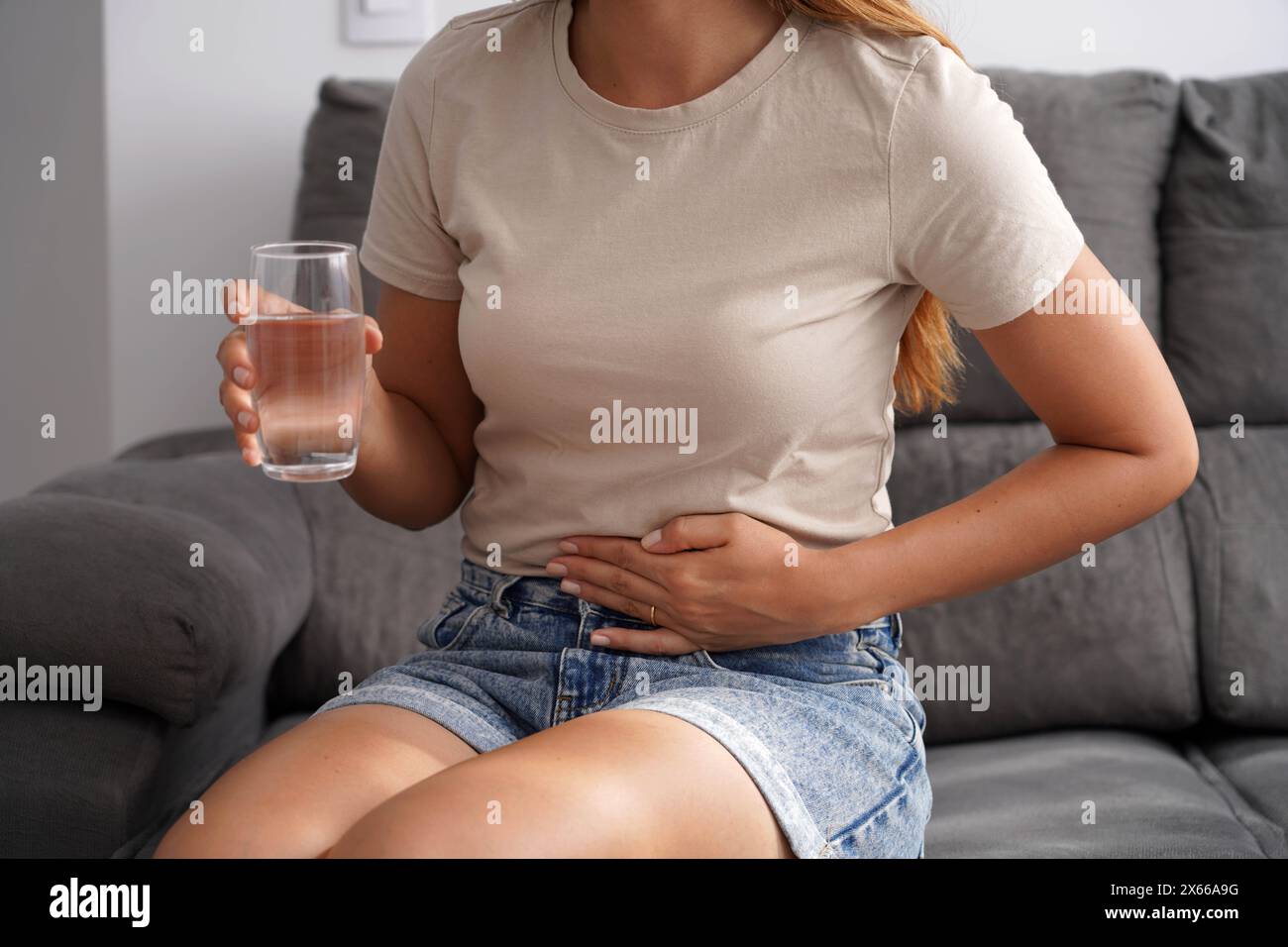 Constipation. Girl suffering from abdominal pain holds a glass of water ...