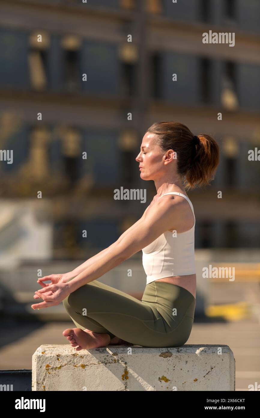woman sitting meditating and relaxing in the sun, urban background ...