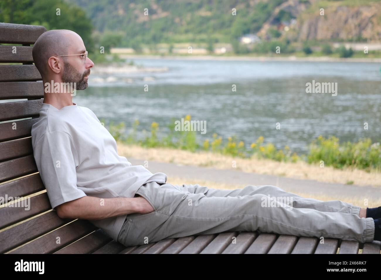 young man 30 years old sites comfortably on wooden park bench on banks ...