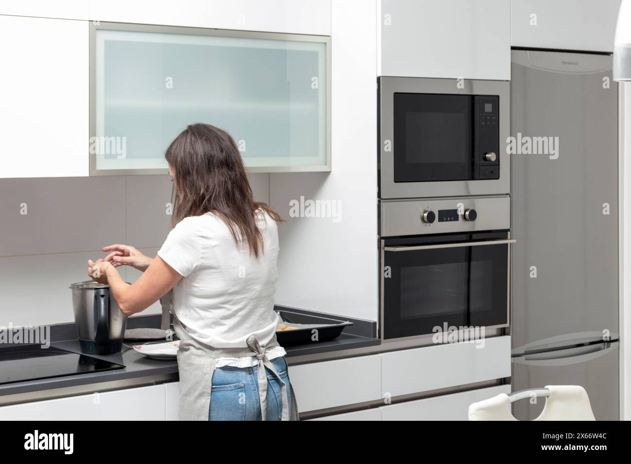 A person in a modern kitchen cooking with a pot on the stove, wearing a ...