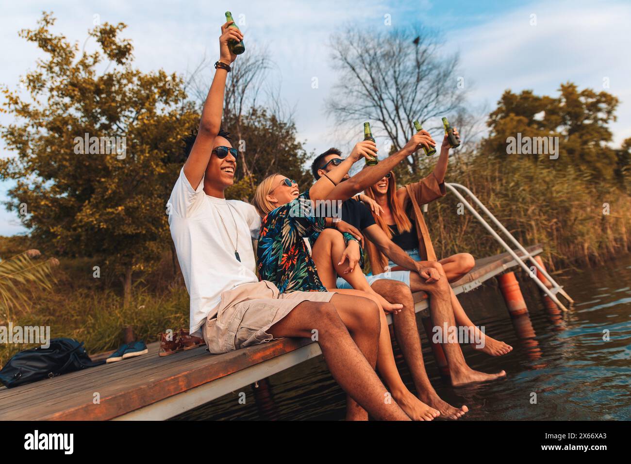 Group of friends enjoying a day at the lake. They sitting on pier ...