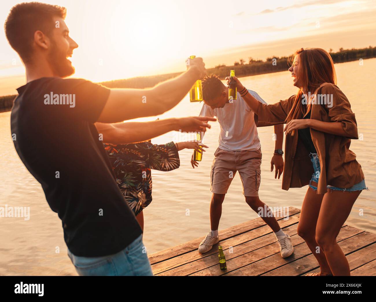 Group of young friends having fun drinking beer and dancing on pier by ...