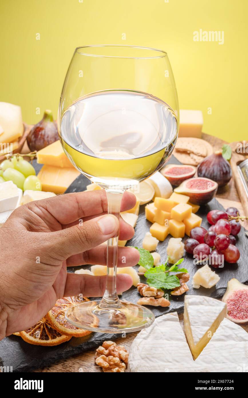 Glass of white wine in a man's hand with variety of sliced cheeses with ...
