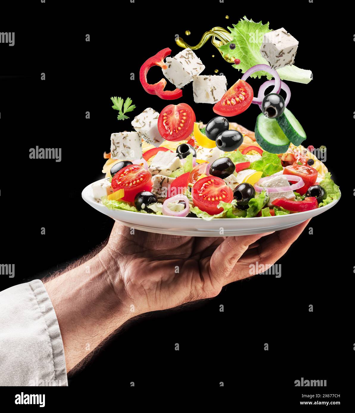 Cook holds white plate of greek salad on black background. Ingredients ...