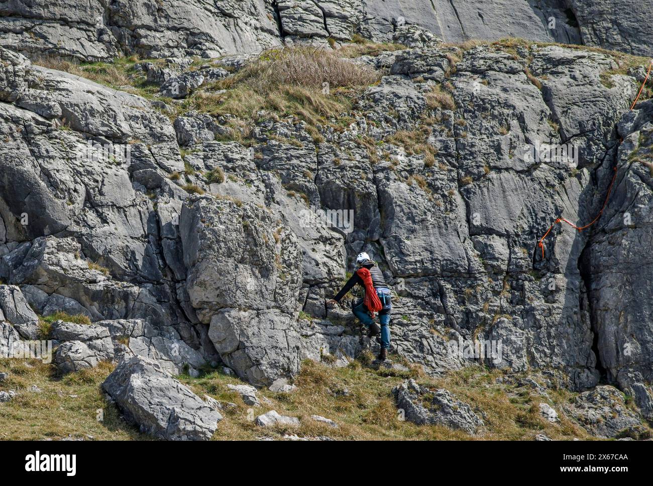 Climber carrying a red rope begining their climb on a limestone cliff ...