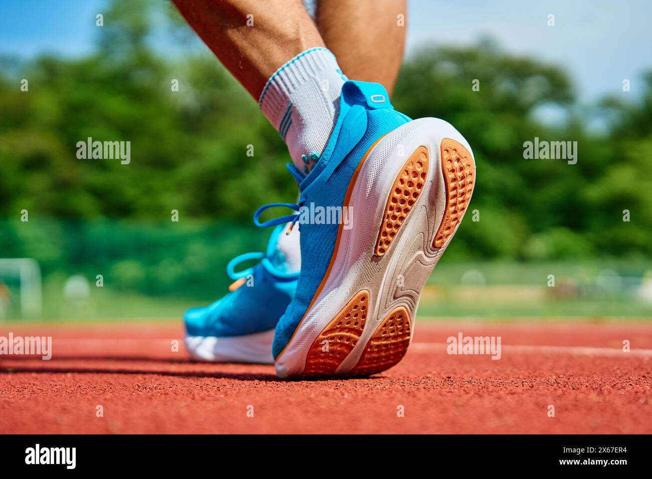 Athlete wearing bright blue running shoes on red stadium track during ...