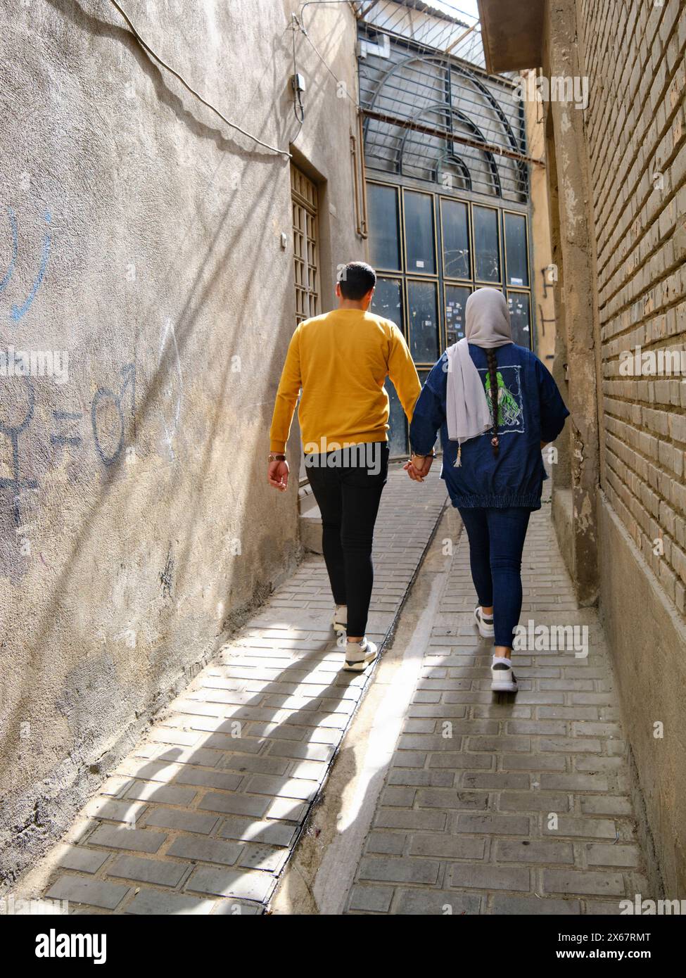 Young Iranian man and woman walk together holding hands in a narrow ...