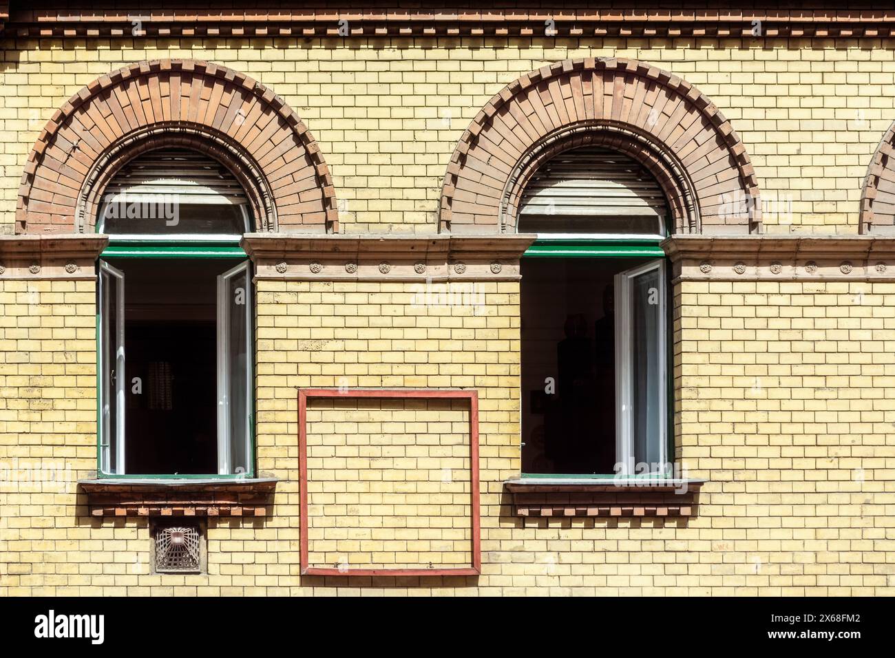 Two rectangular arched windows with open frames against a yellow brick ...