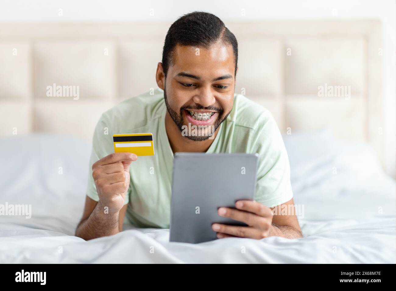 Man Laying on Bed With Credit Card and Tablet Stock Photo - Alamy