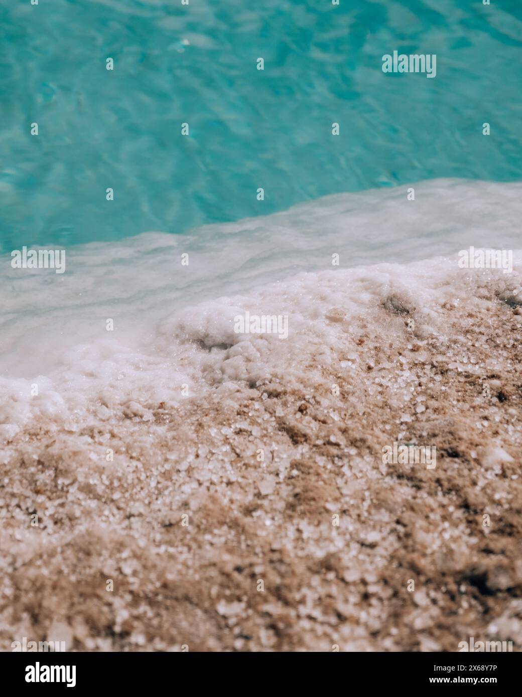 Close-up of crystalline salt deposits on the shore of a turquoise salt ...