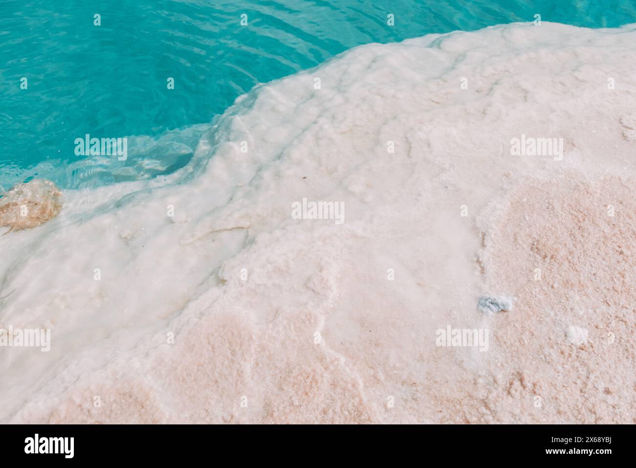 Close-up of crystalline salt deposits on the shore of a turquoise salt ...