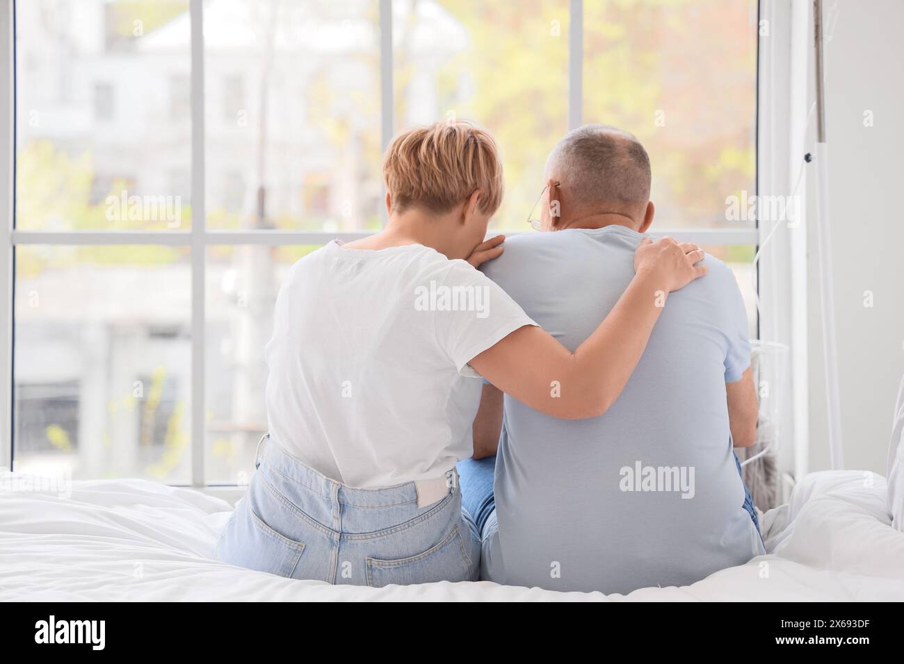 Mature woman hugging her sick husband with infusion drip in bedroom ...