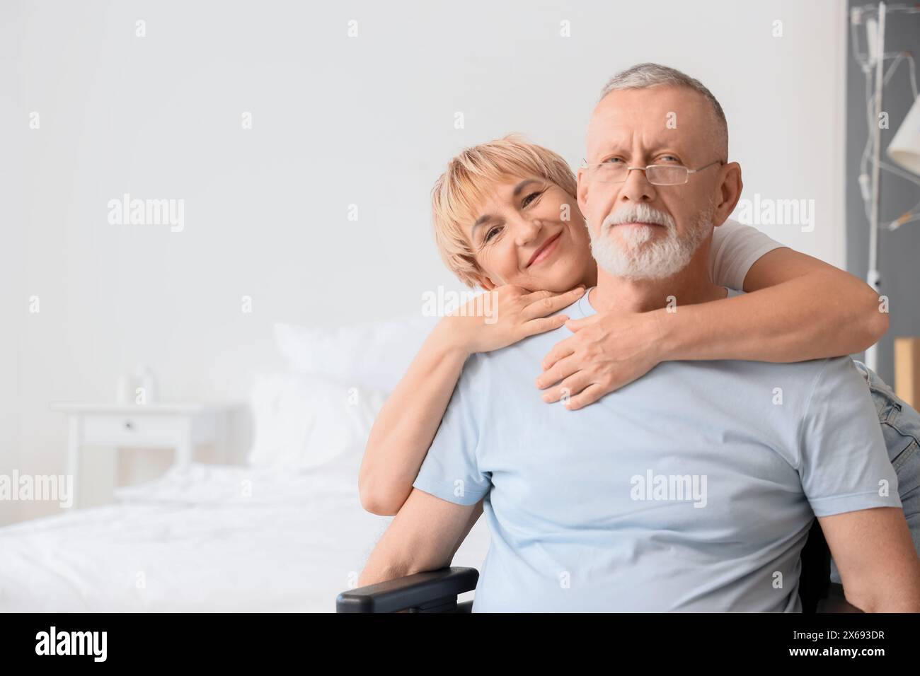 Mature woman hugging her sick husband in wheelchair at home Stock Photo ...