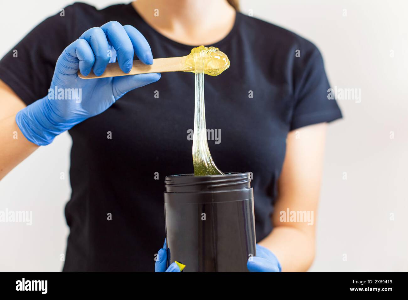 Professional sugarist holdind black jar mixing wax with a stick close ...