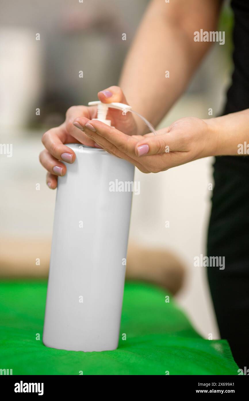 Closeup of a masseur pouring oil to her hand in a bright massage spa ...