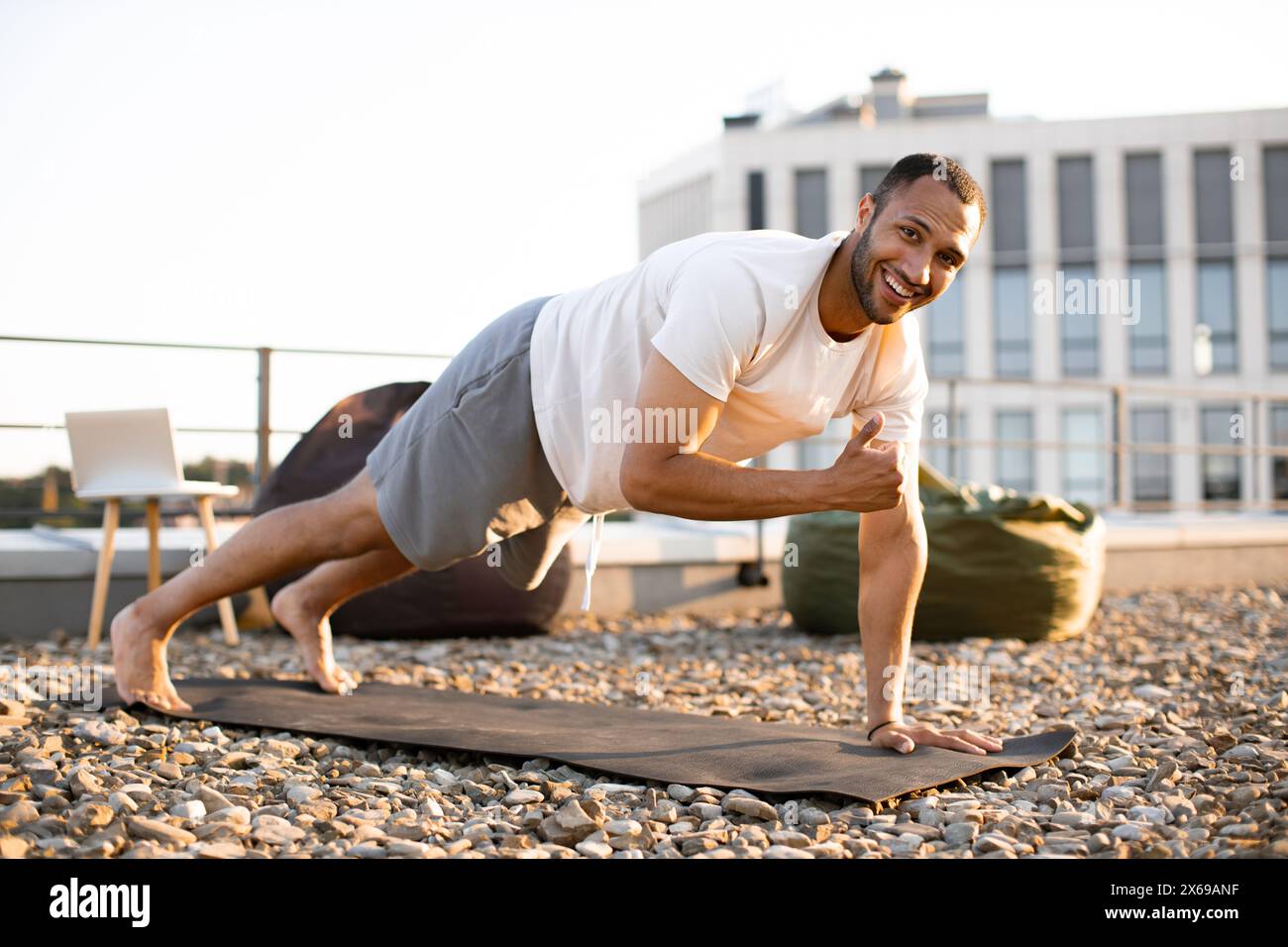 Strong male in plank position on mat during sunrise against urban ...