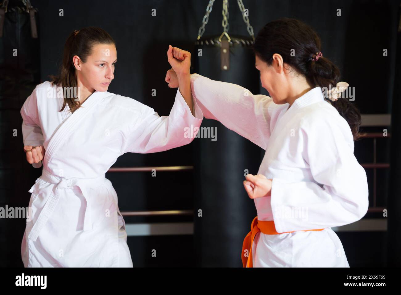Portrait of woman wearing white kimono sparring with female opponent during martial arts ...