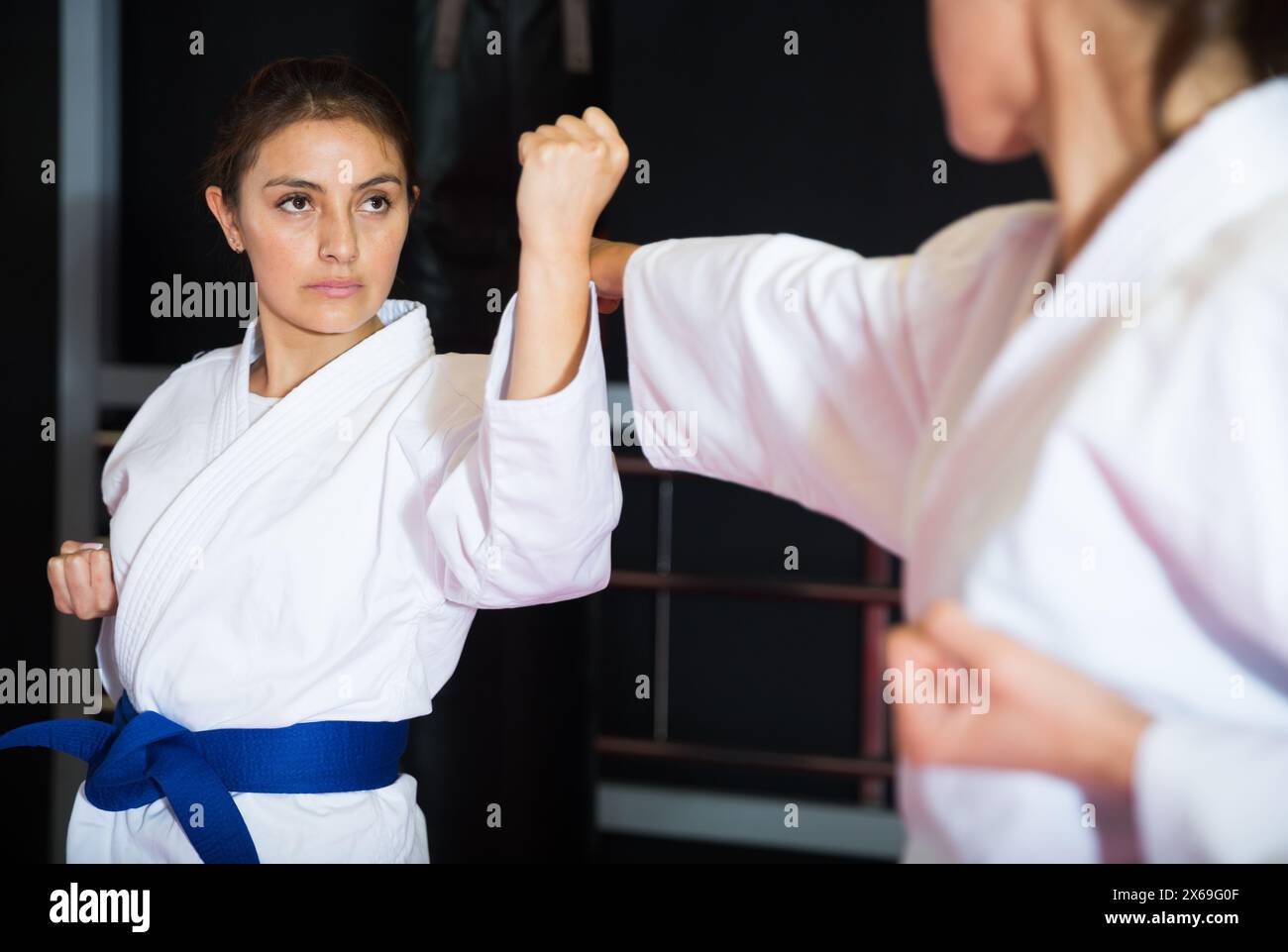 Portrait of woman wearing white kimono sparring with female opponent during martial arts ...