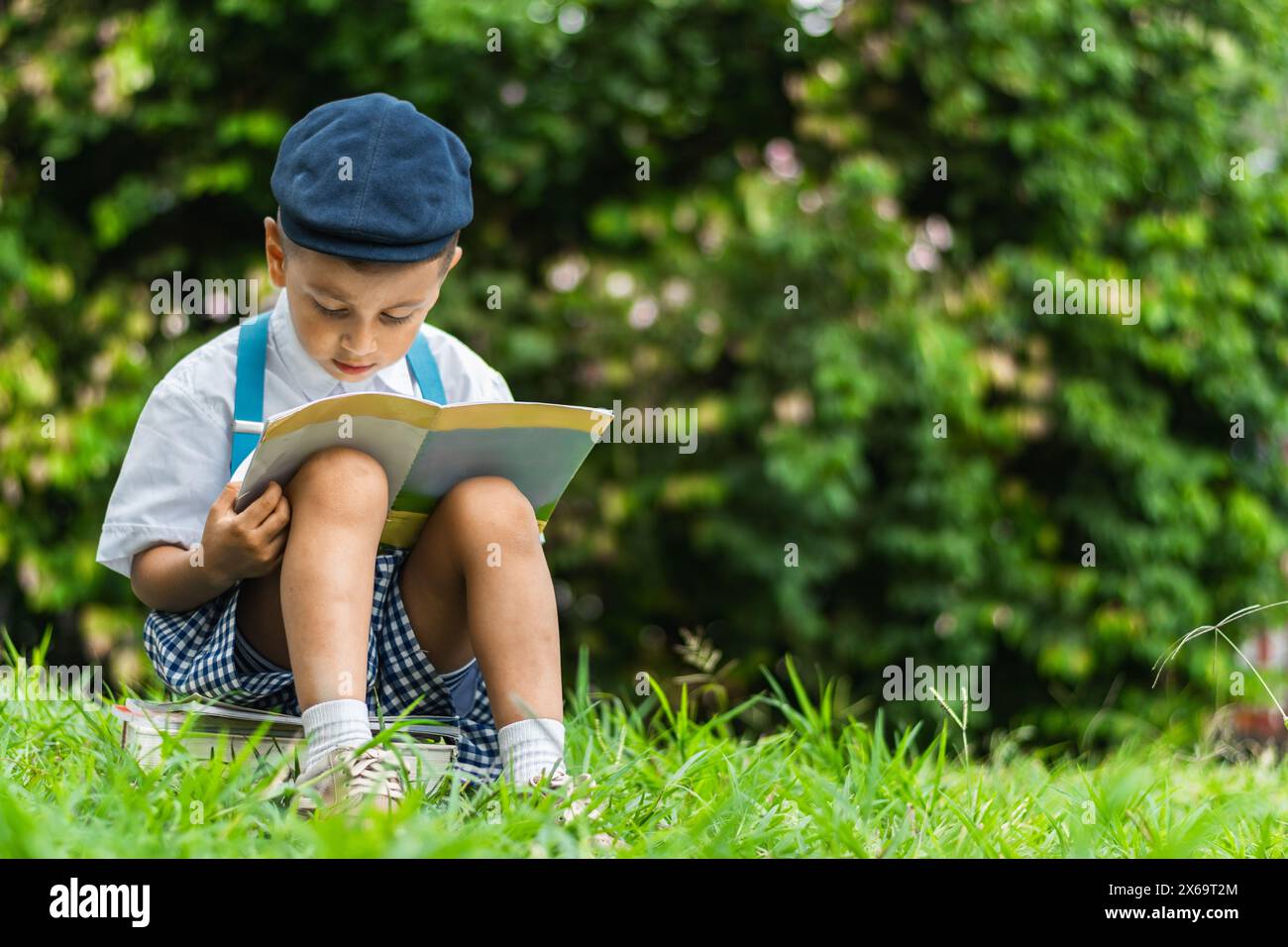 little Latino boy sitting in the park reading a book, very concentrated ...