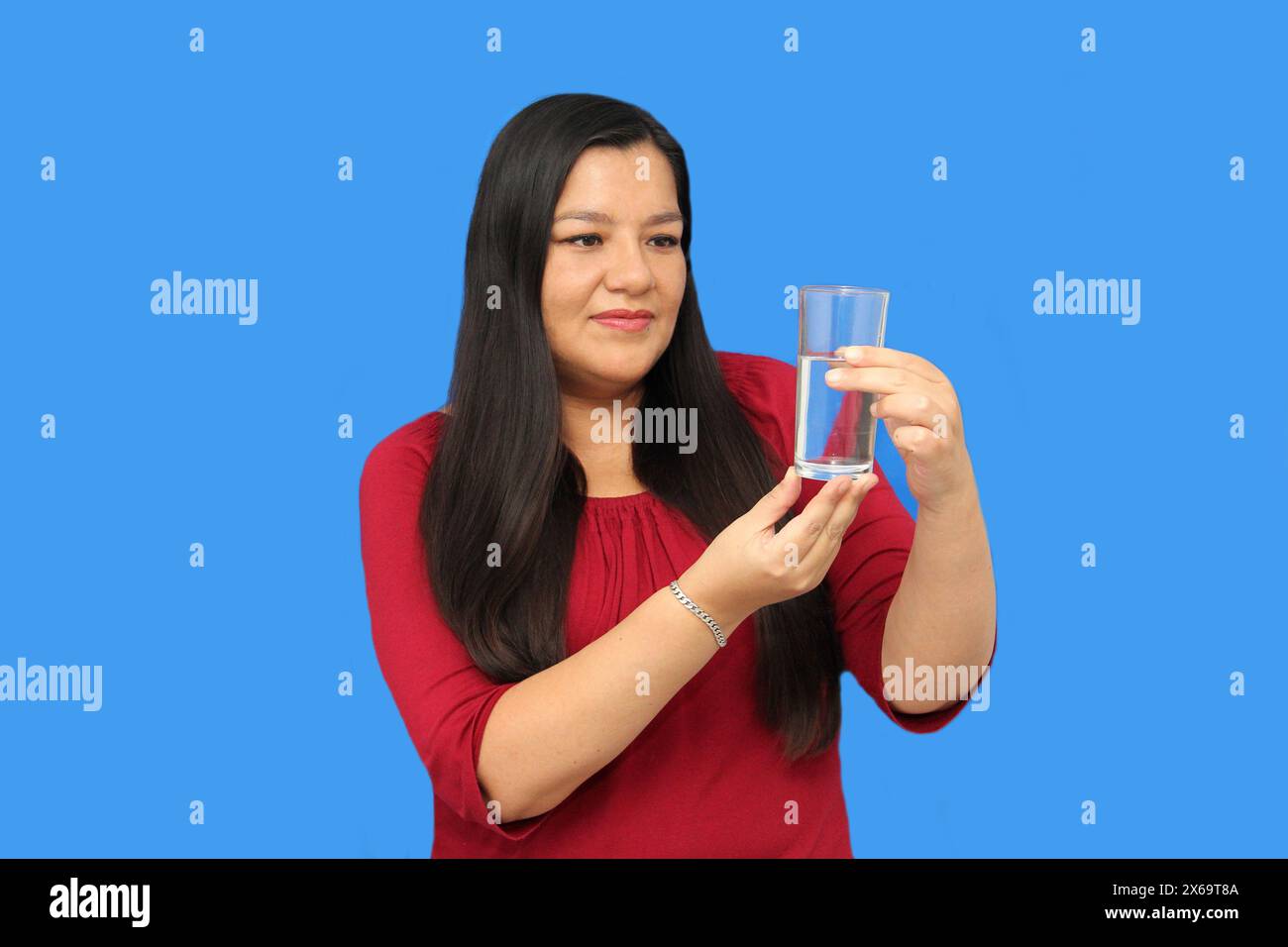 Latin adult woman shows a glass cup with drinking water that she drinks ...