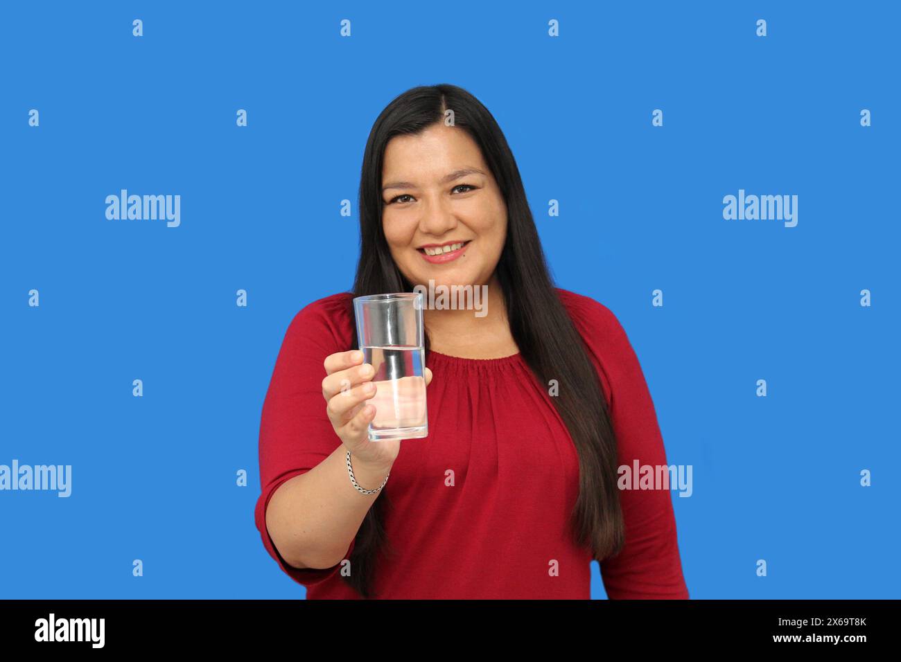 Latin adult woman shows a glass cup with drinking water that she drinks ...