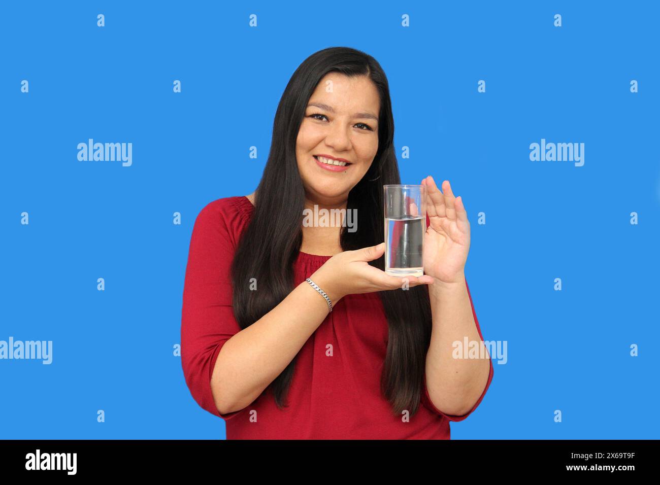 Latin adult woman shows a glass cup with drinking water that she drinks ...