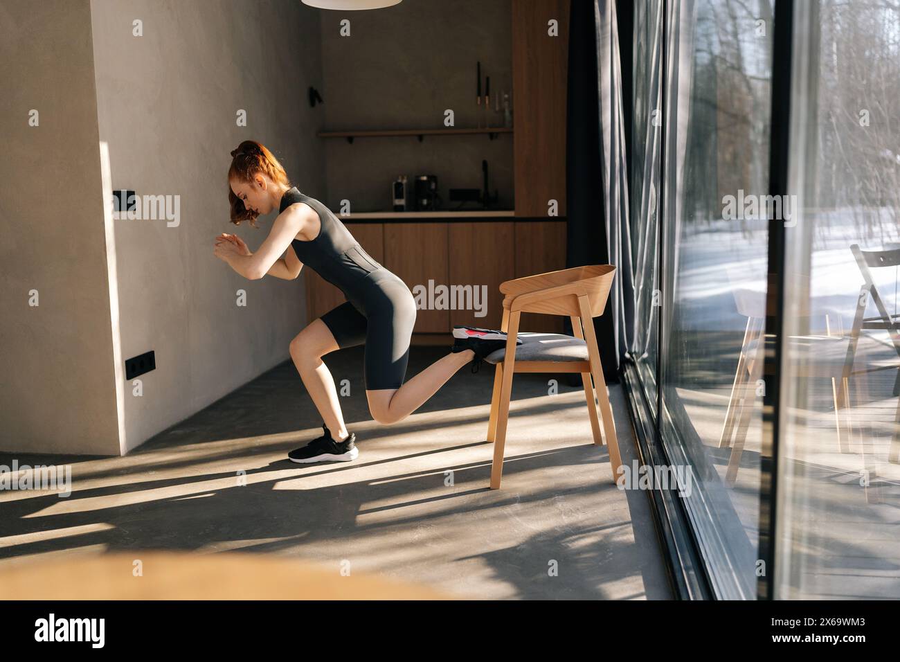 Side view of fit slim female doing single leg lunge using chair in ...