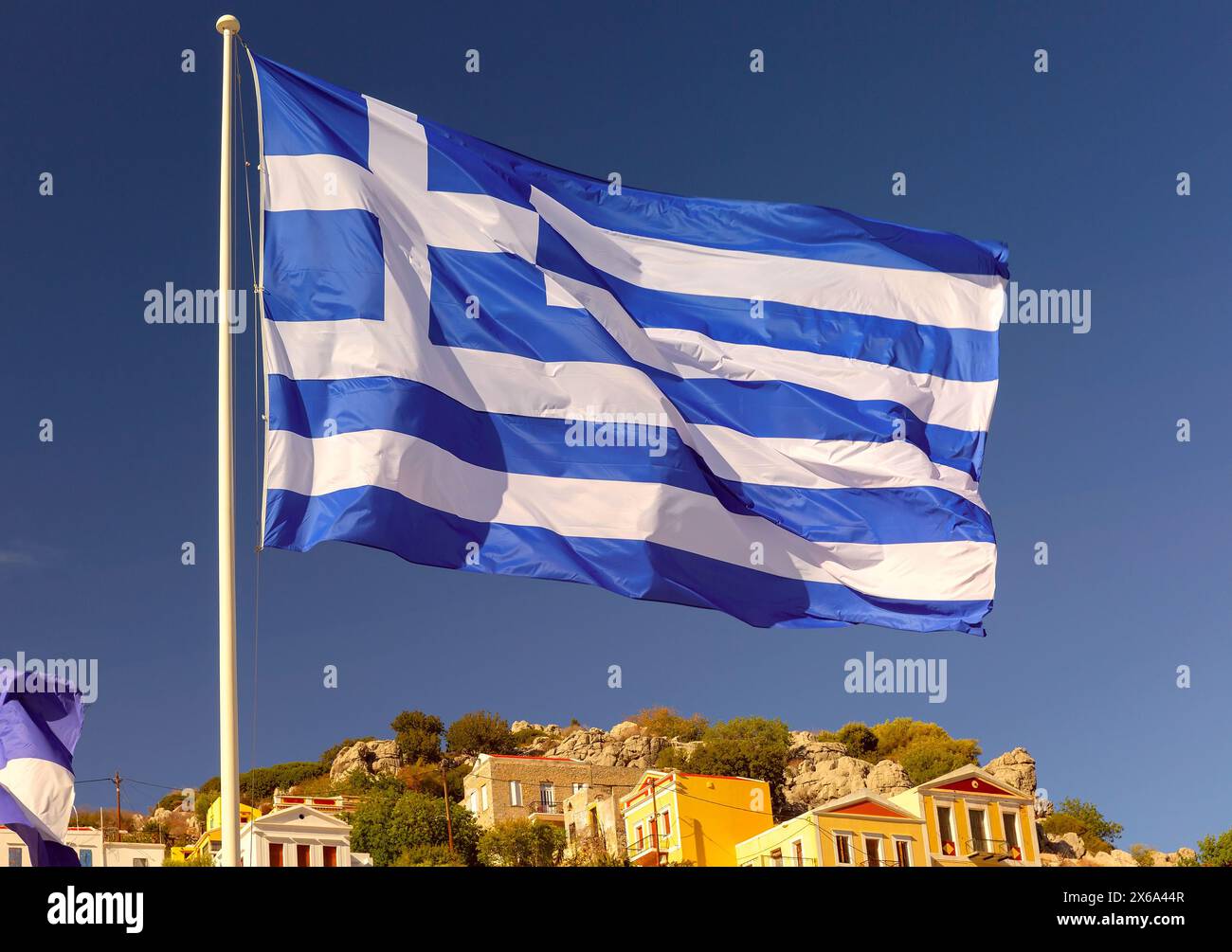 Vibrant Greek flag fluttering above colorful houses of charming Greek ...