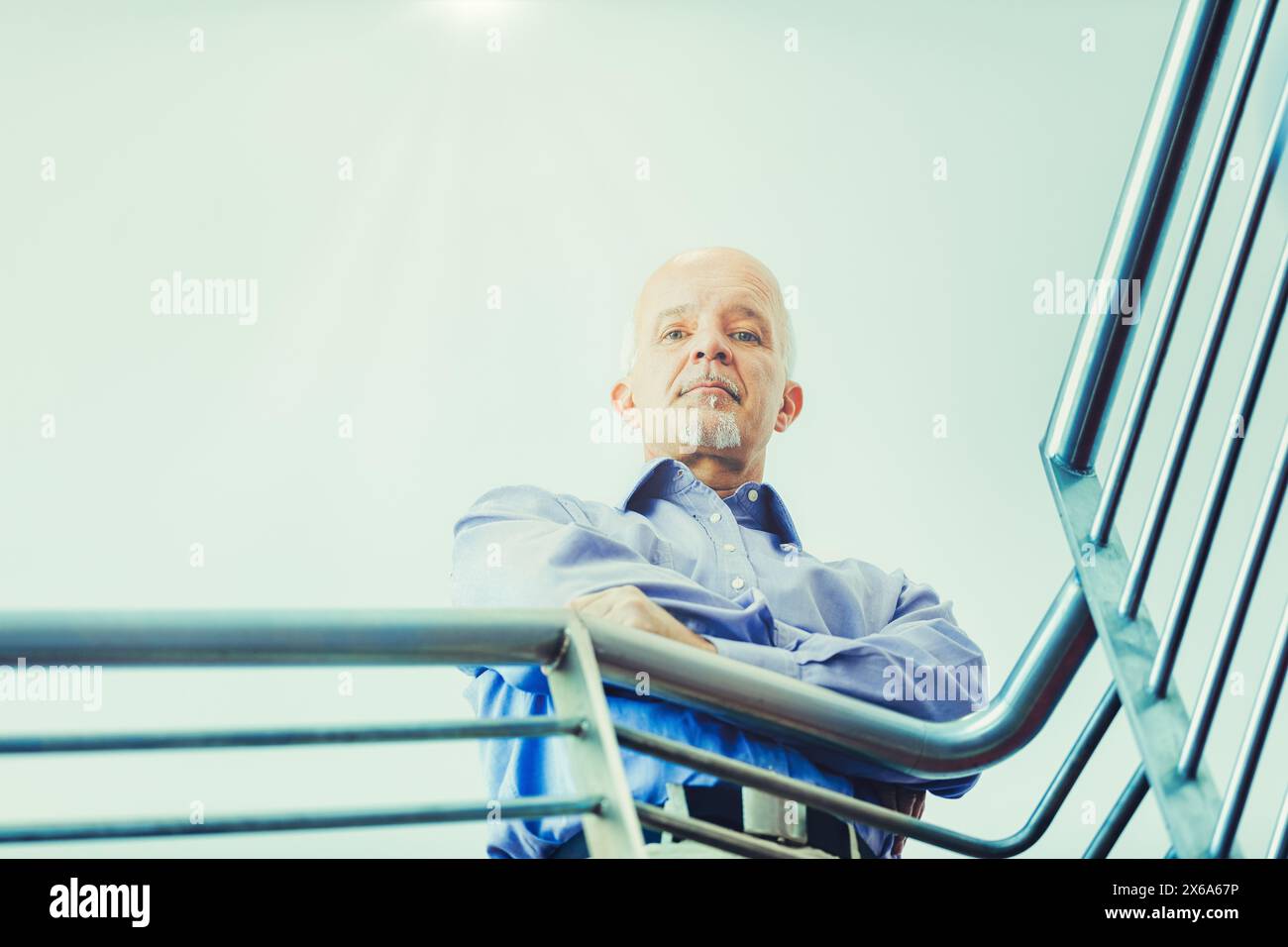 Mature man with authoritative gaze stands over camera, blue shirt ...