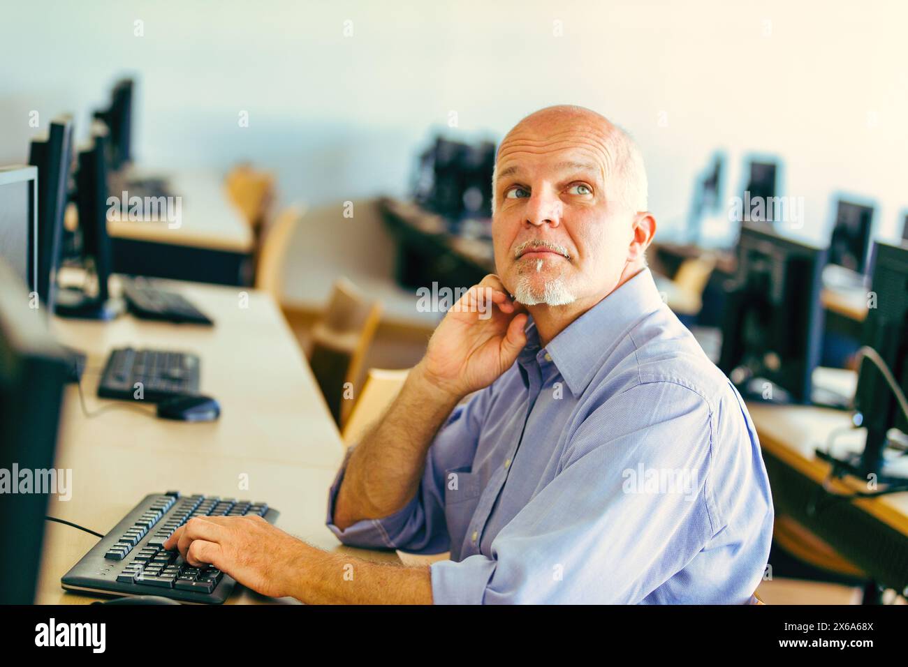 In a computer lab, an older man with a grey beard and contemplative ...