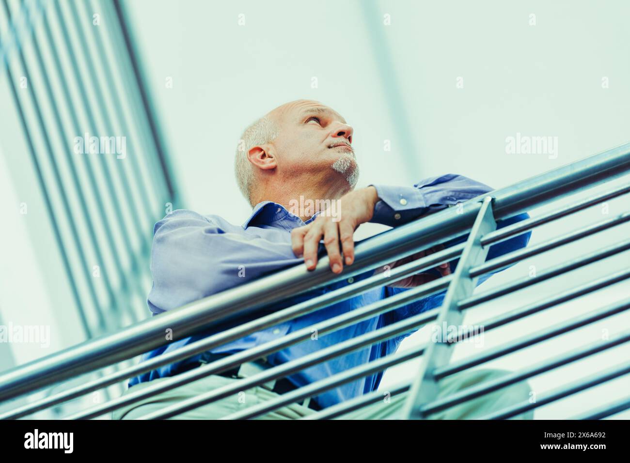 Elderly man with a contemplative look leans on a metal railing, gazing ...