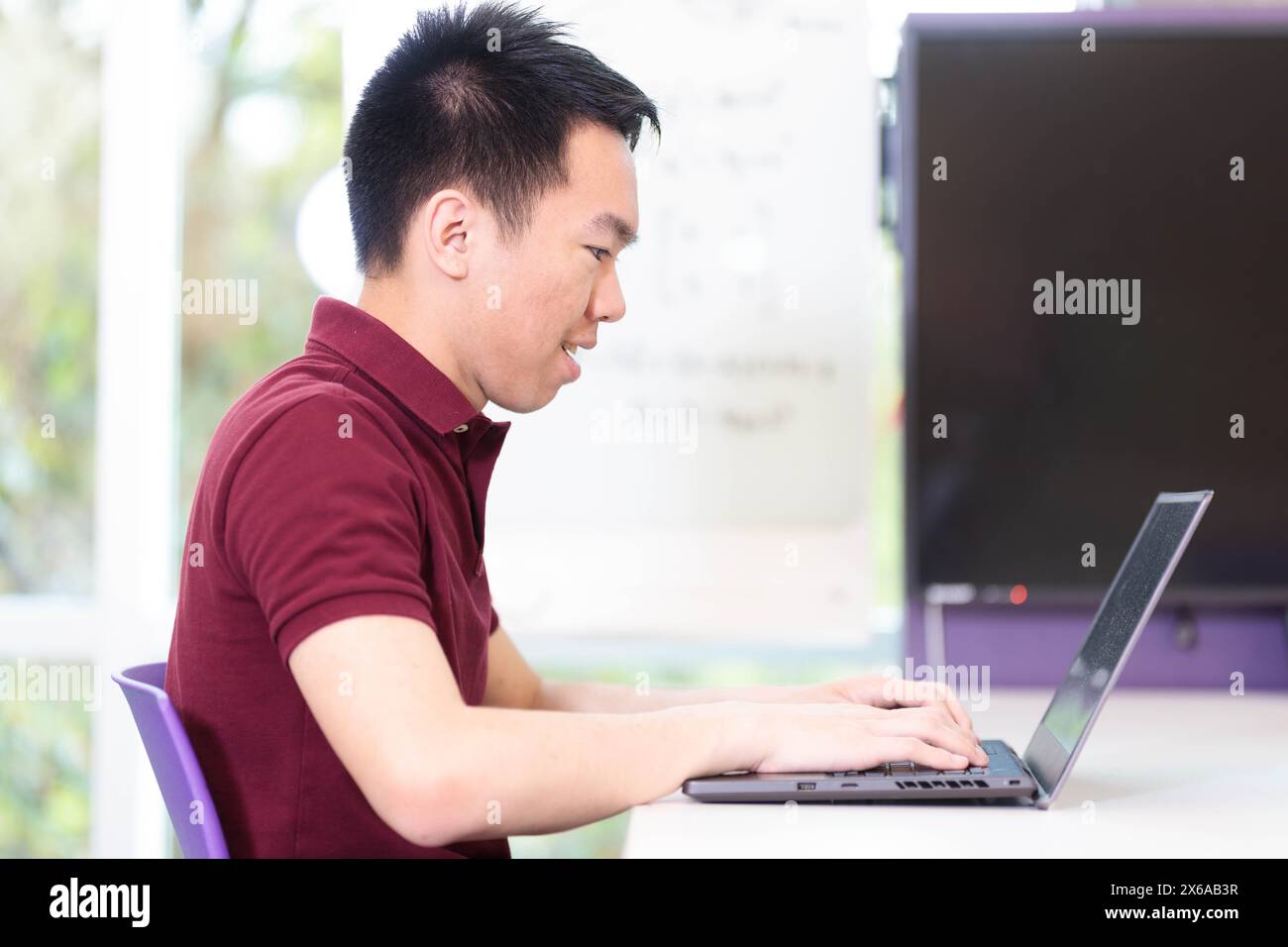 A young male university student is comfortably seated at a desk ...