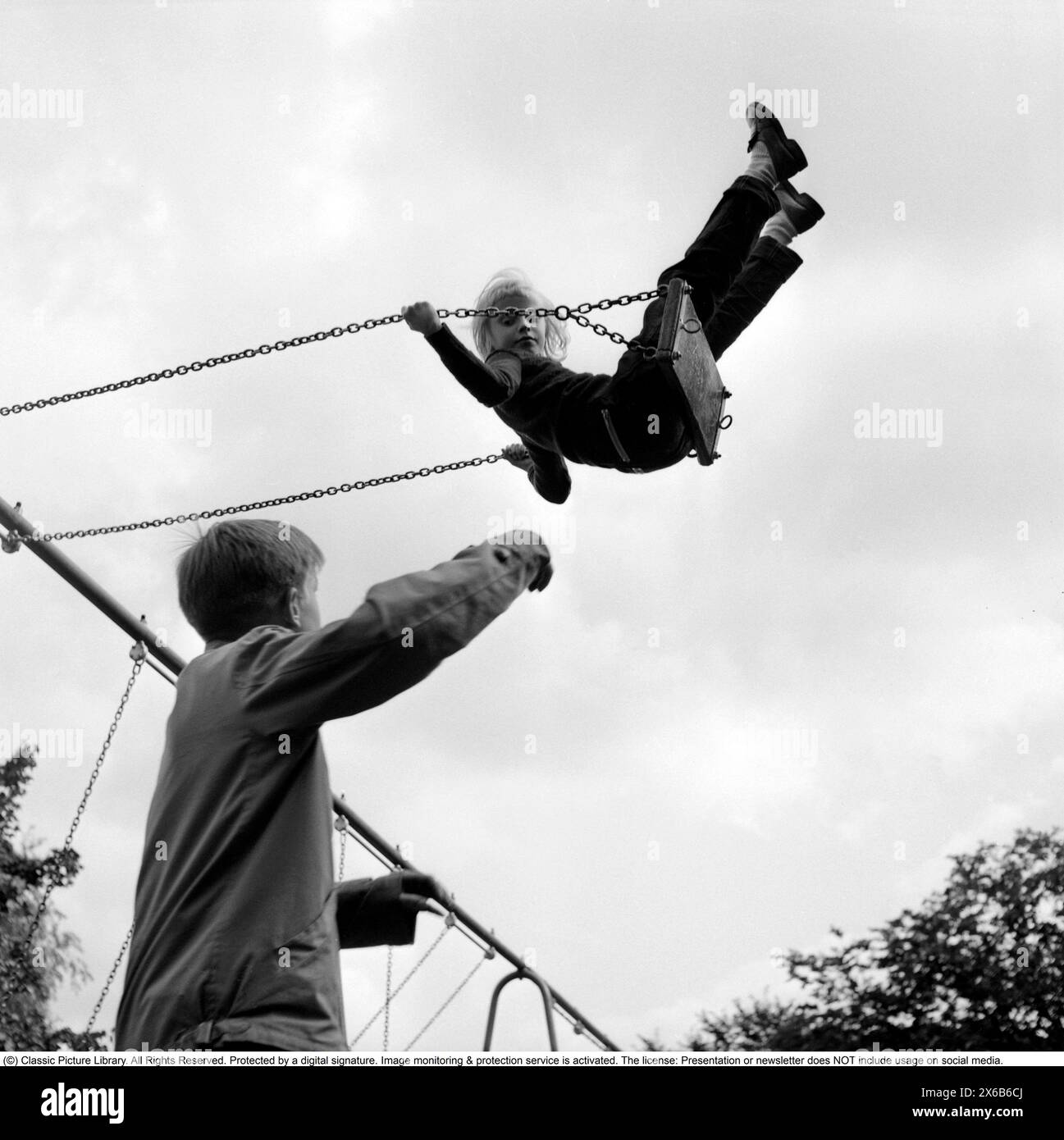 In the 1950s. A child pictured in a swing, full speed upwards, having ...
