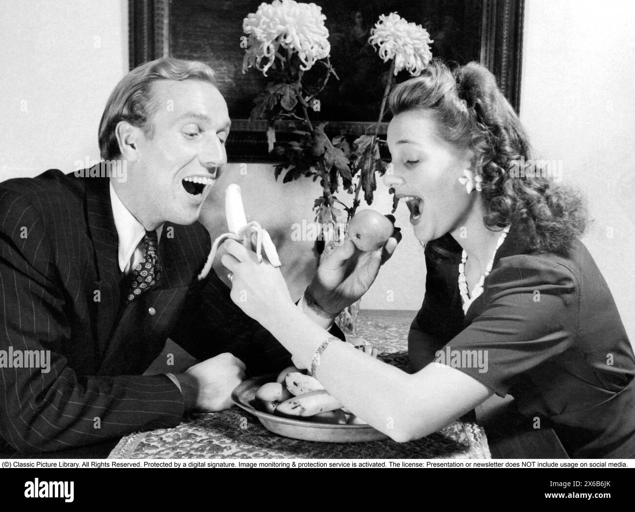 Couple at the table in 1946. They are holding a banana and an apple in ...
