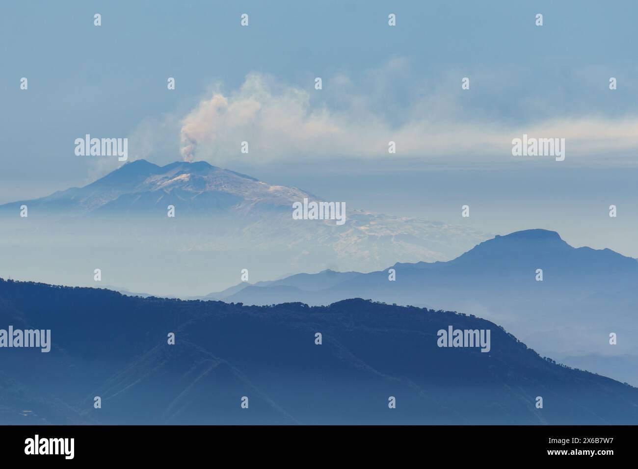 Smoke rising up from active Etna volcano at Sicily on a hazy blue day ...