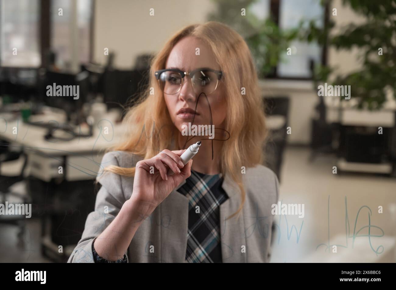 Caucasian woman with glasses writes text in English on a glass wall ...