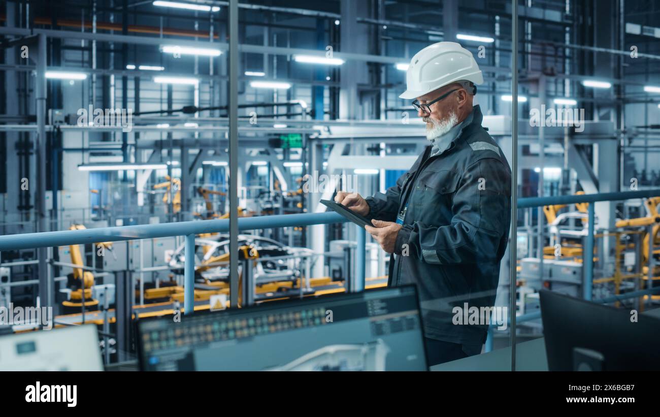 Car Factory: Male Automotive Engineer Wearing Hard Hat, Standing Using Tablet Computer ...