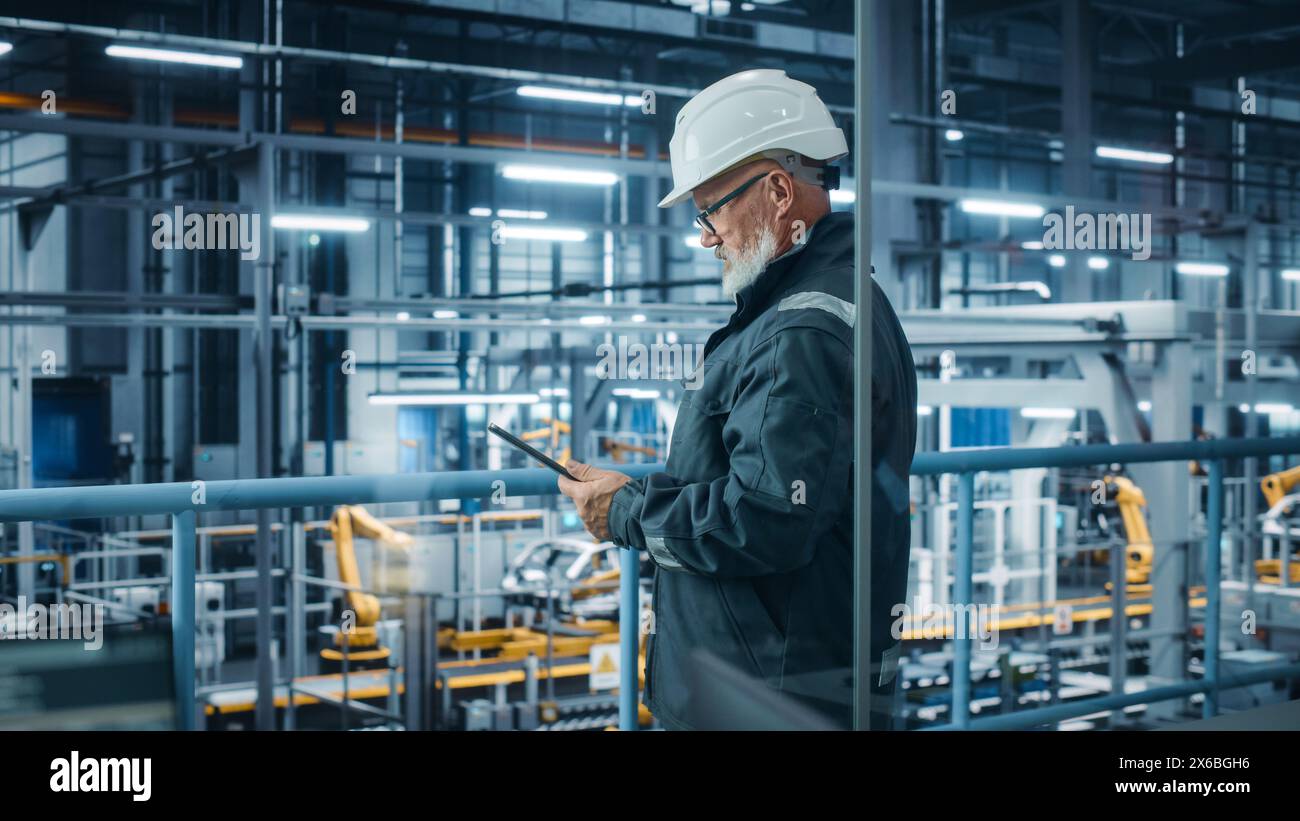 Car Factory: Male Automotive Engineer Wearing Hard Hat, Standing Using Tablet Computer ...