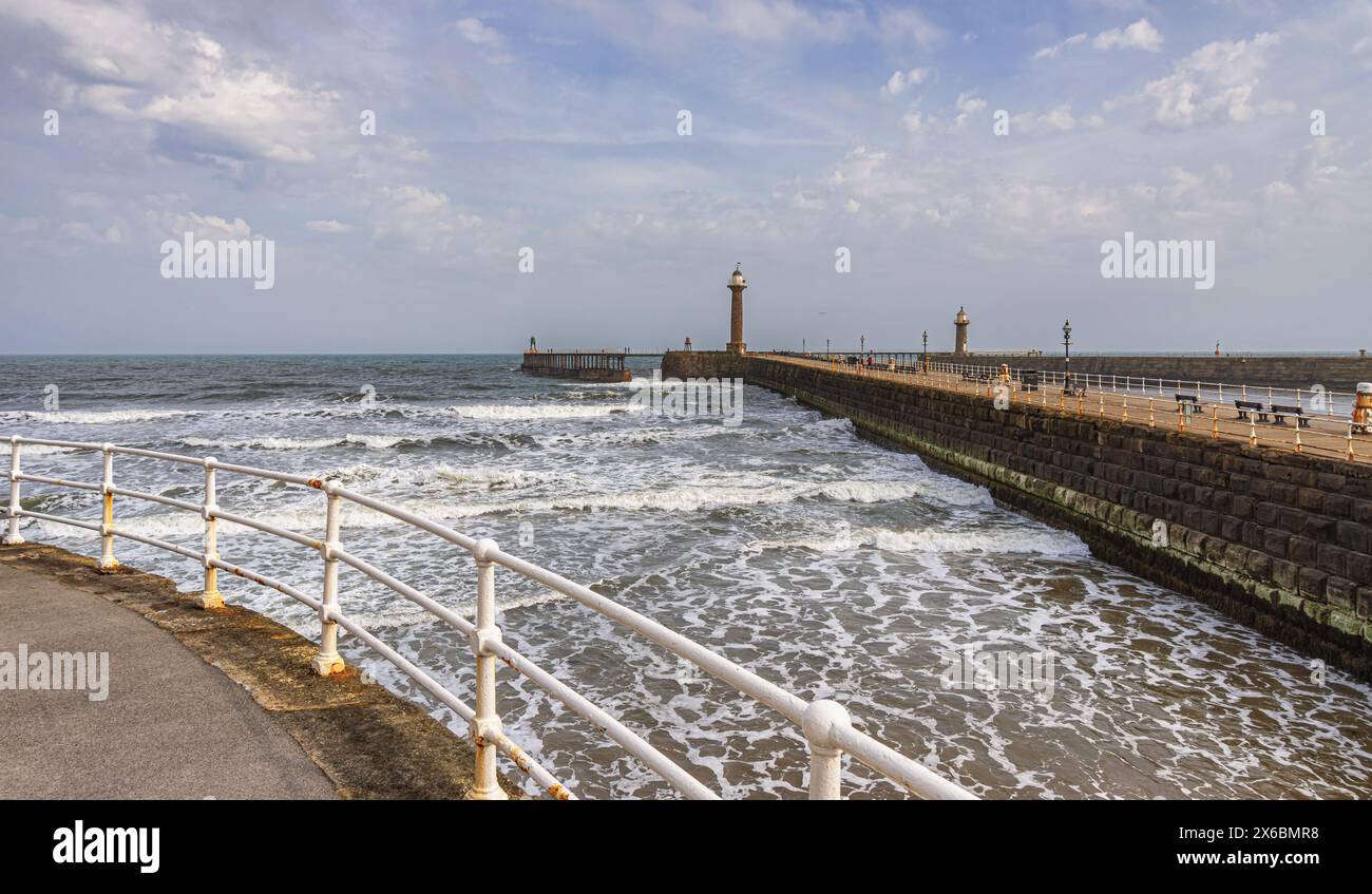 A pier with a lighthouse stretches out into a stormy sea while waves ...