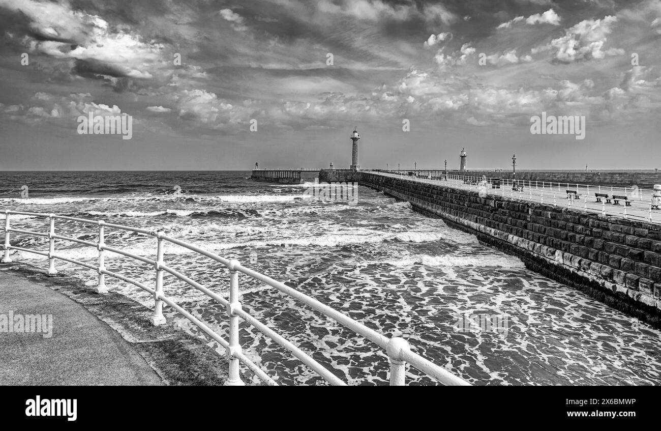 A pier with a lighthouse stretches out into a stormy sea while waves ...