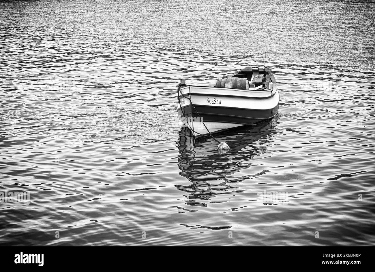 A lone boat is moored to a buoy in a harbour. A barrel is positioned in ...