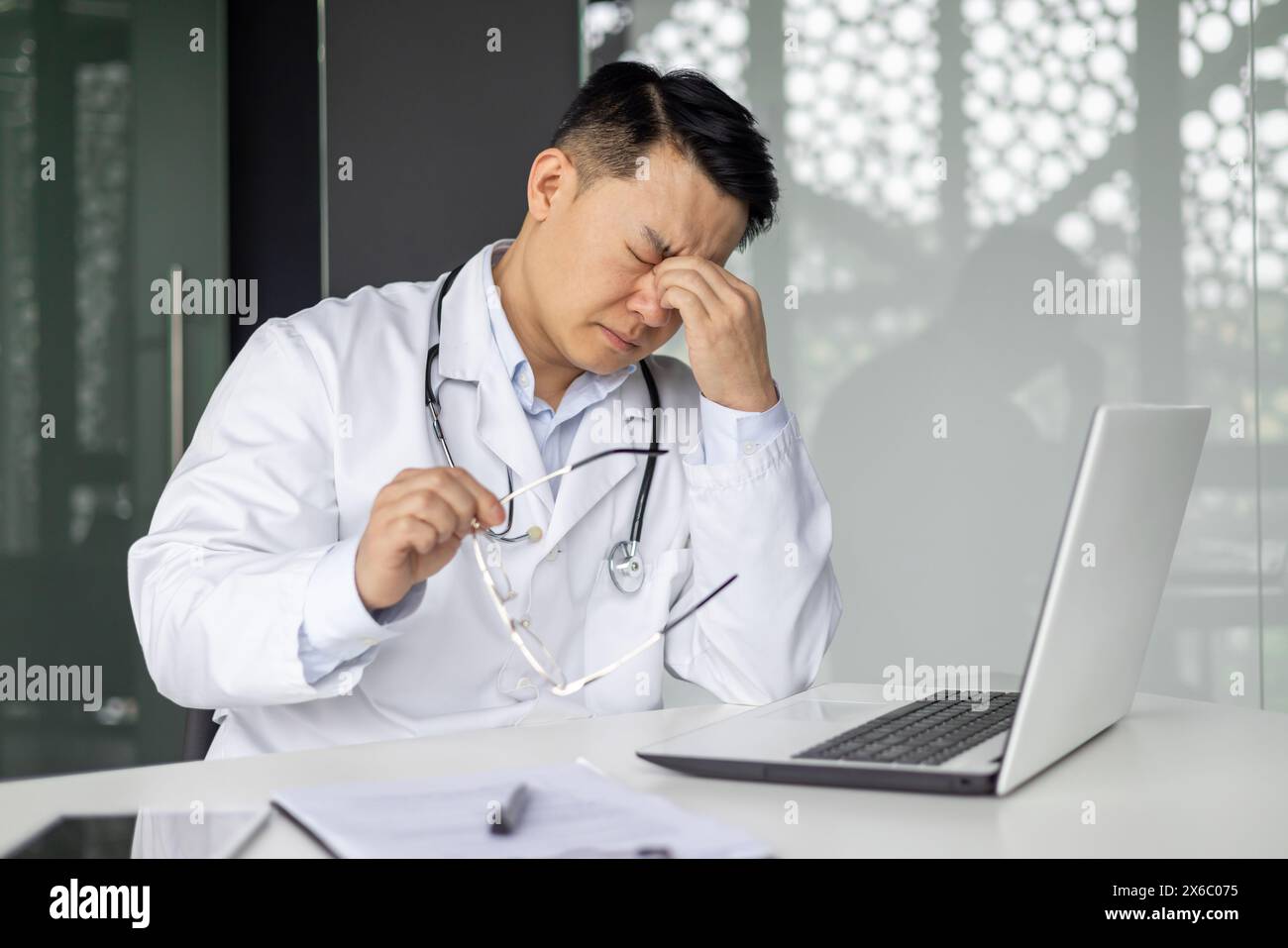 Asian mature doctor looking stressed while sitting at desk with laptop ...