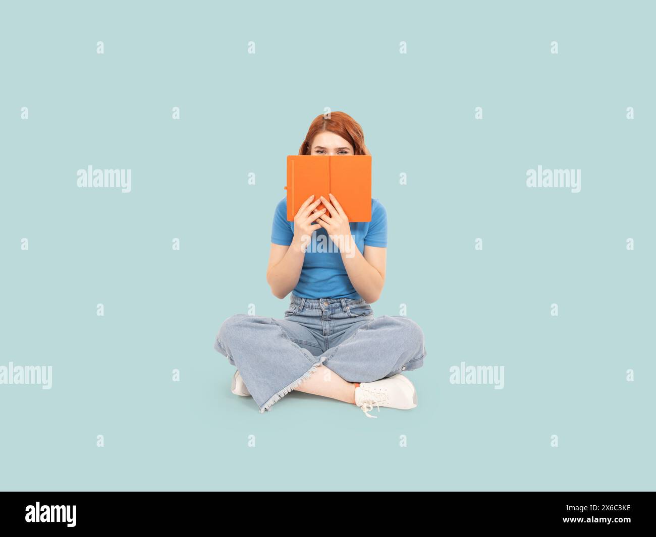 Reading book, full body length portrait of caucasian red hair woman sit floor legs crossed ...