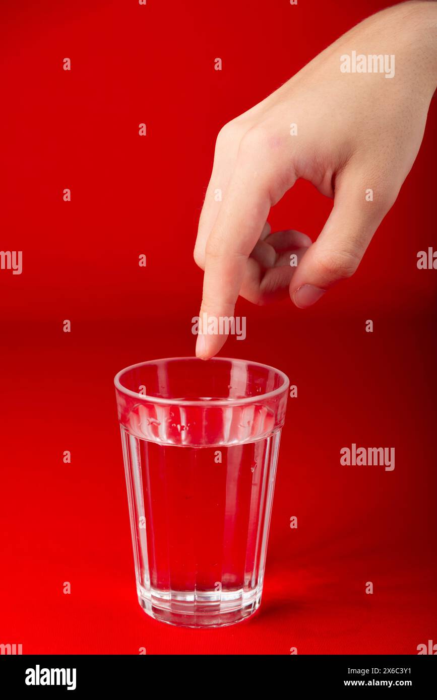 Male hand pointing to the water inside a transparent glass cup ...