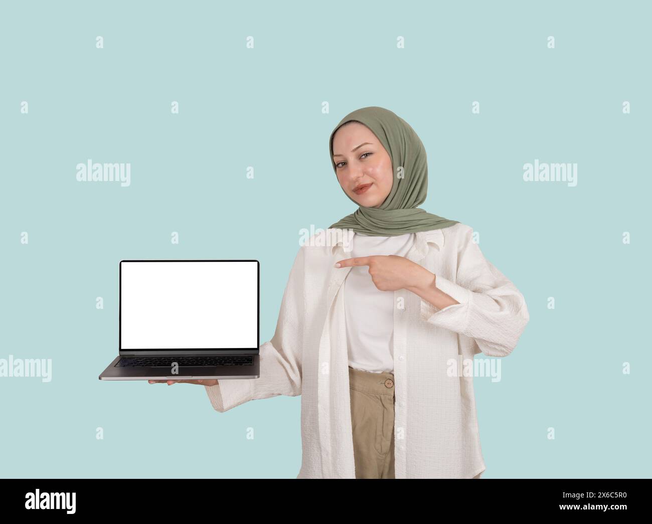 portrait of excited caucasian muslim girl in hijab presenting laptop ...