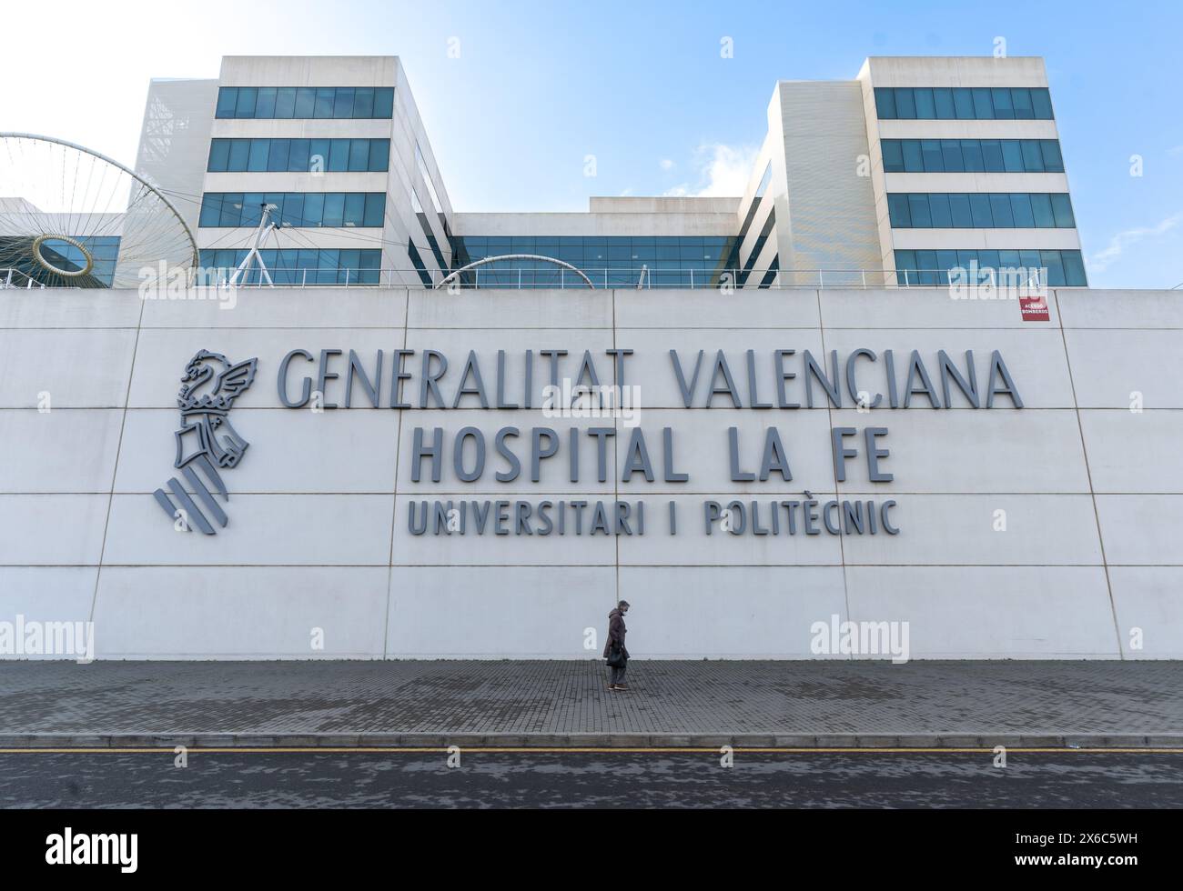 A person wearing a mask walks past the large sign of the Valencian ...